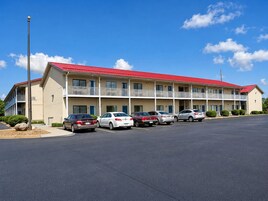 Um motel com teto vermelho, vários andares e estacionamento com diversos carros.