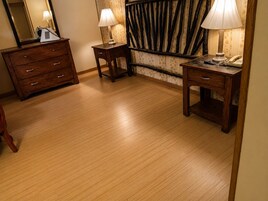 Quarto de hotel com cômoda de madeira, duas mesas de cabeceira com luminárias, um espelho e parede estampada.