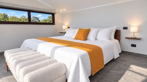Quarto moderno com cama grande, um banco e vista para o verde lá fora.