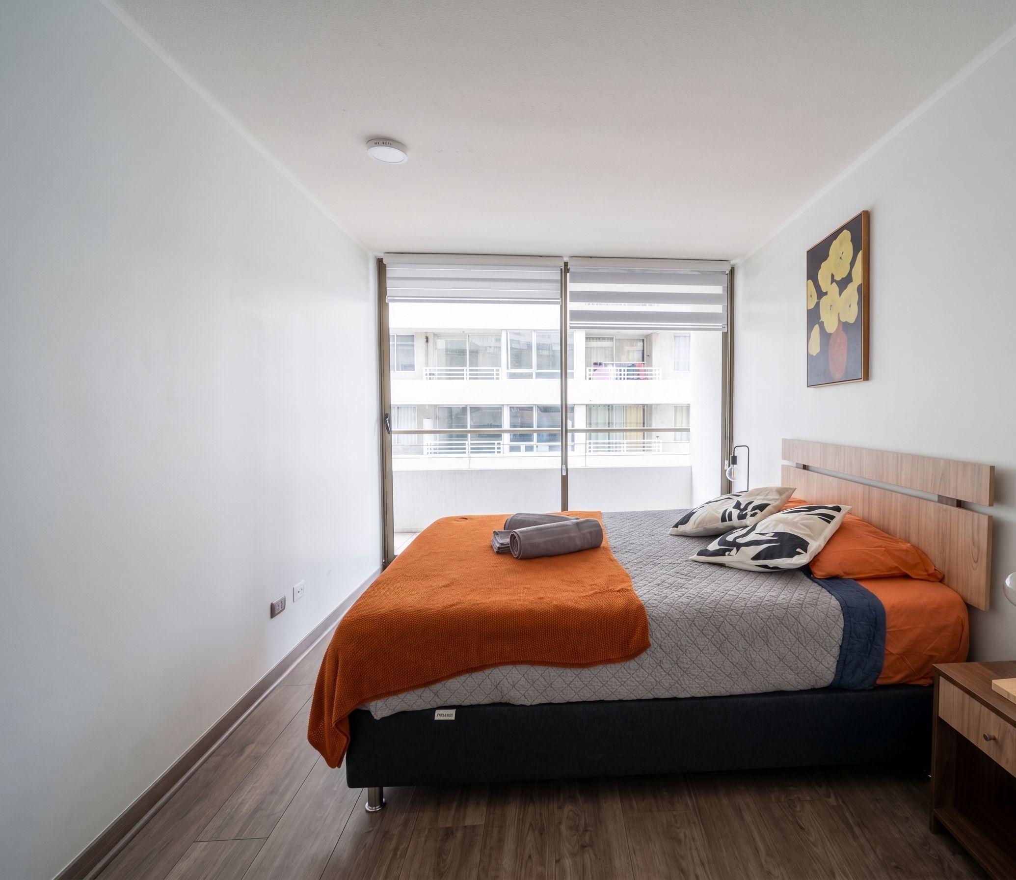 Quarto com cama, mesa de cabeceira, janela e pintura na parede.