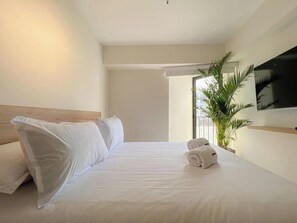 Quarto de hotel com cama, almofadas, uma planta e televisão na parede.