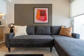 Uma sala de estar moderna com um sofá seccional cinza, uma obra de arte abstrata emoldurada na parede e uma mesa de centro.