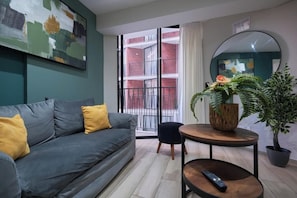 Uma sala de estar moderna com um sofá cinza, uma mesa de centro redonda de madeira e um vaso com planta.