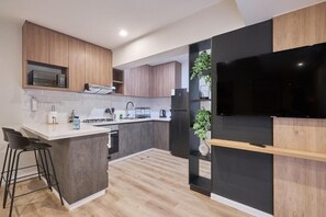 Cozinha moderna com ilha central, armários de madeira, uma TV preta e uma planta.