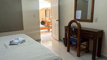 Quarto com cama, escrivaninha, cadeira, televisão fixada na parede e porta que dá para outro cômodo.