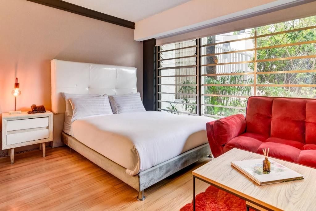 Quarto moderno com cama, mesa de cabeceira e um sofá vermelho.