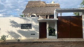Um edifício moderno com telhado de palha, uma placa com a inscrição 'Casa Linda' e uma entrada com portão.