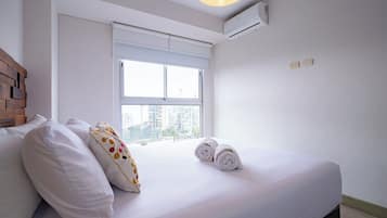 Quarto de hotel com cama, almofadas, janela e vista para prédios.
