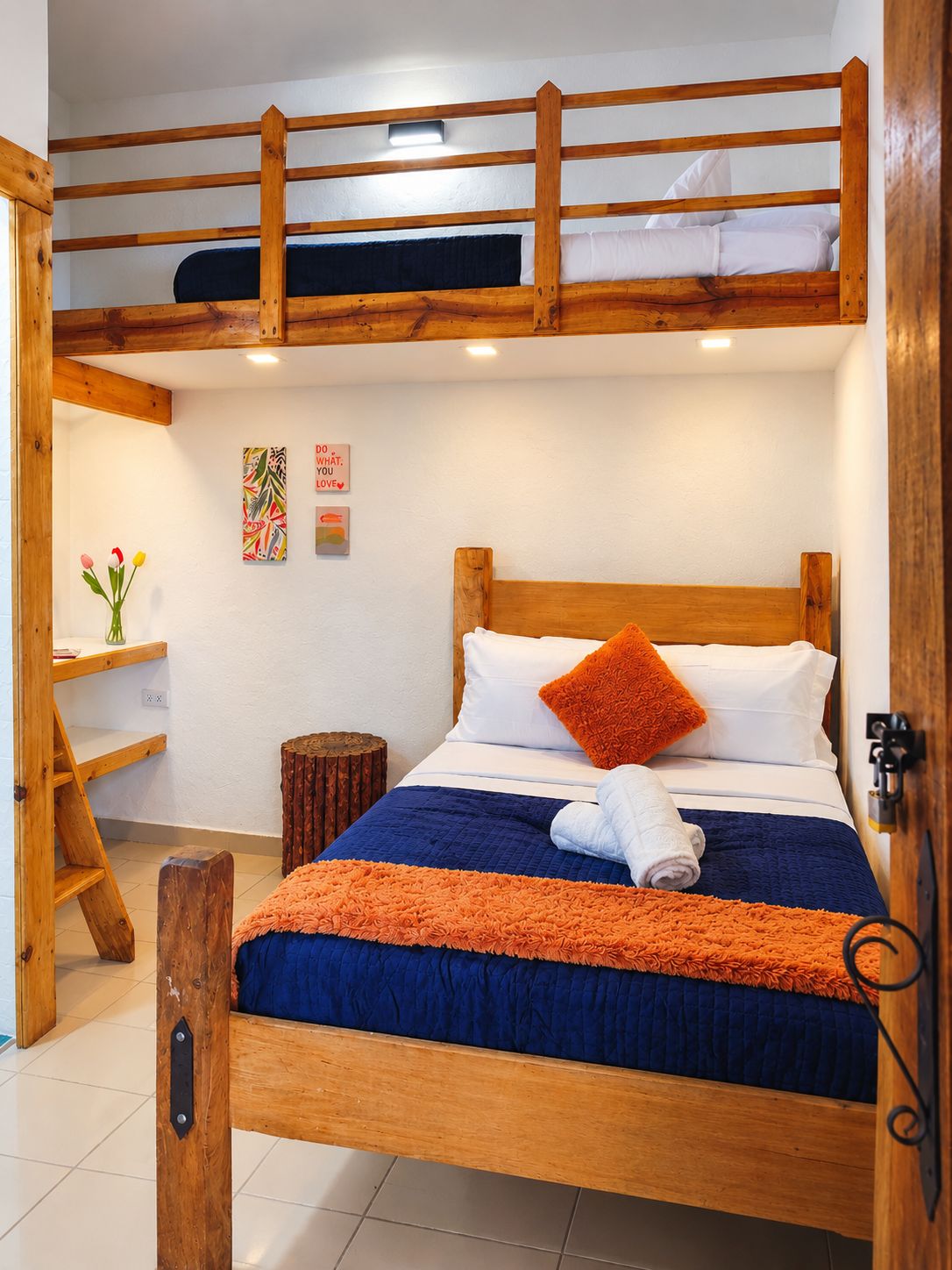 Uma cama beliche com estrutura de madeira, edredom azul e laranja, e travesseiro branco.