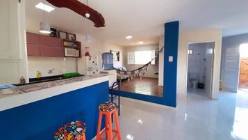 Uma sala ampla com cozinha, uma rede e dois banquinhos coloridos.