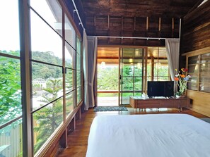Quarto com cama grande, TV e vista para o verde lá fora.