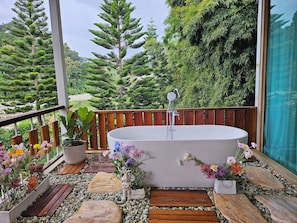 Uma área de spa com banheira de imersão, rodeada por um deck de madeira, plantas em vasos e um caminho de pedras.