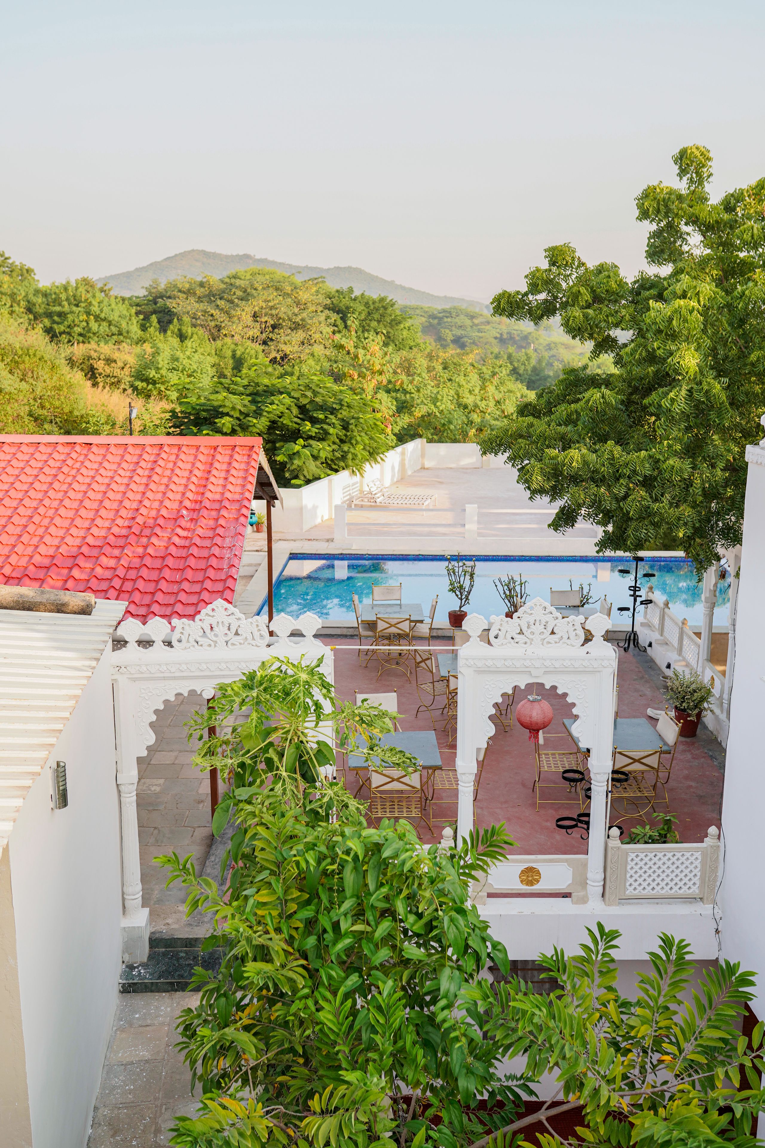 Área de piscina com teto vermelho, colunas brancas e mobiliário para área externa.