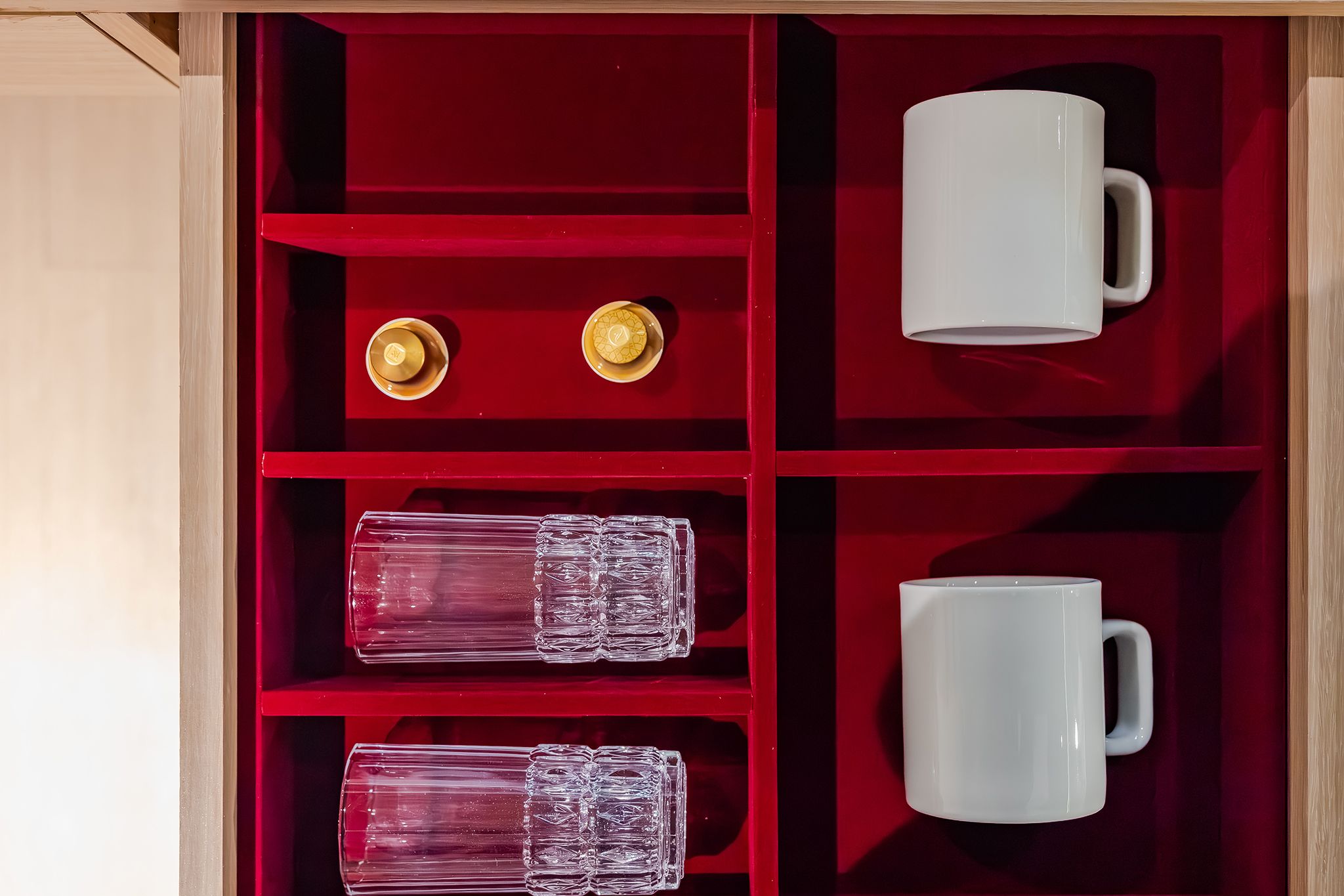 Um armário vermelho com duas alças douradas, dois recipientes de vidro transparente e dois copos brancos.
