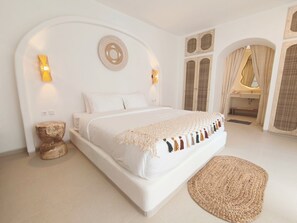 Quarto moderno com uma cama grande, um tapete redondo de fibra natural e banheiro com pia e espelho.