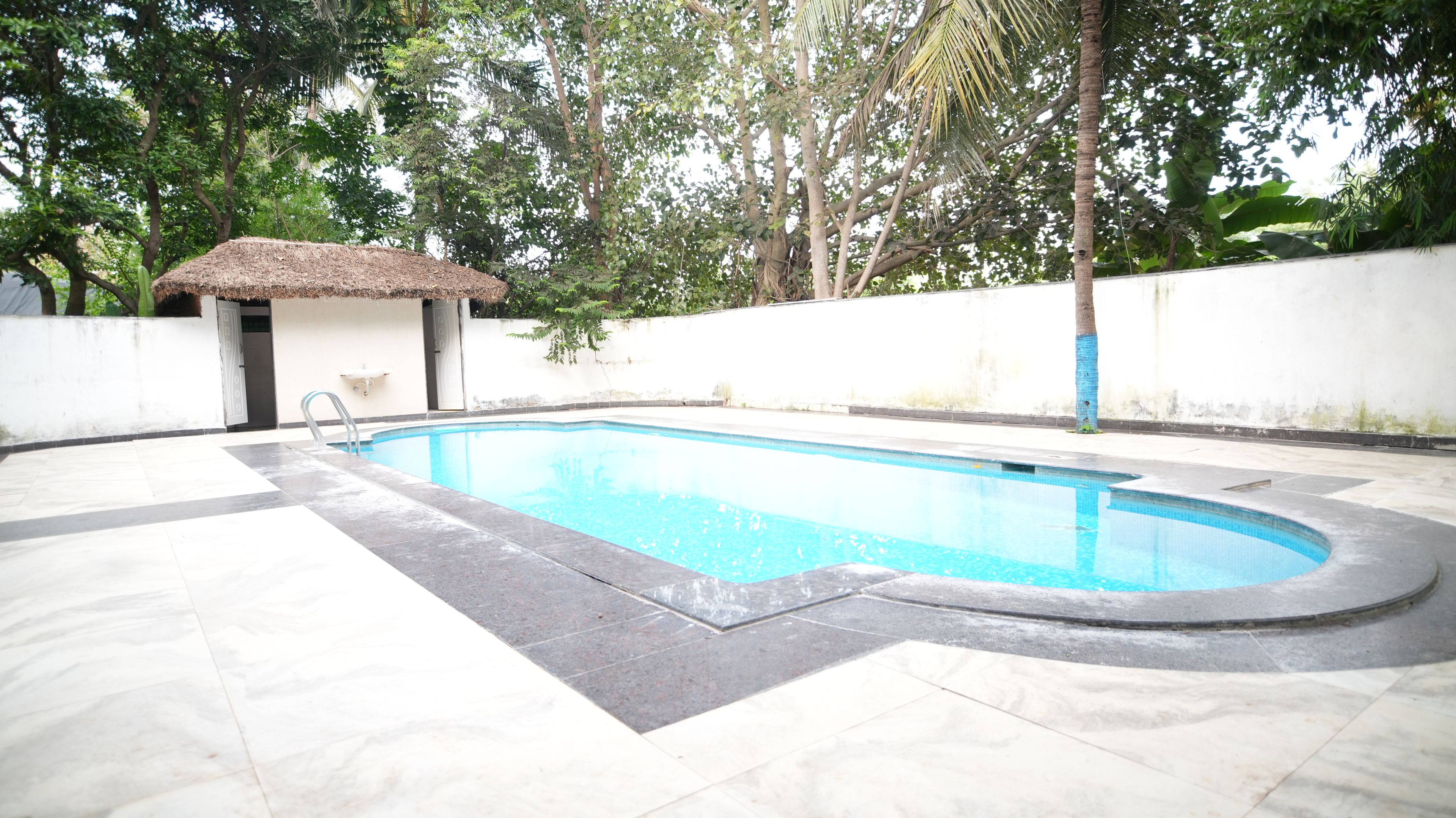 Piscina com deck de azulejos, uma pequena cabana e uma parede branca com detalhes azuis.