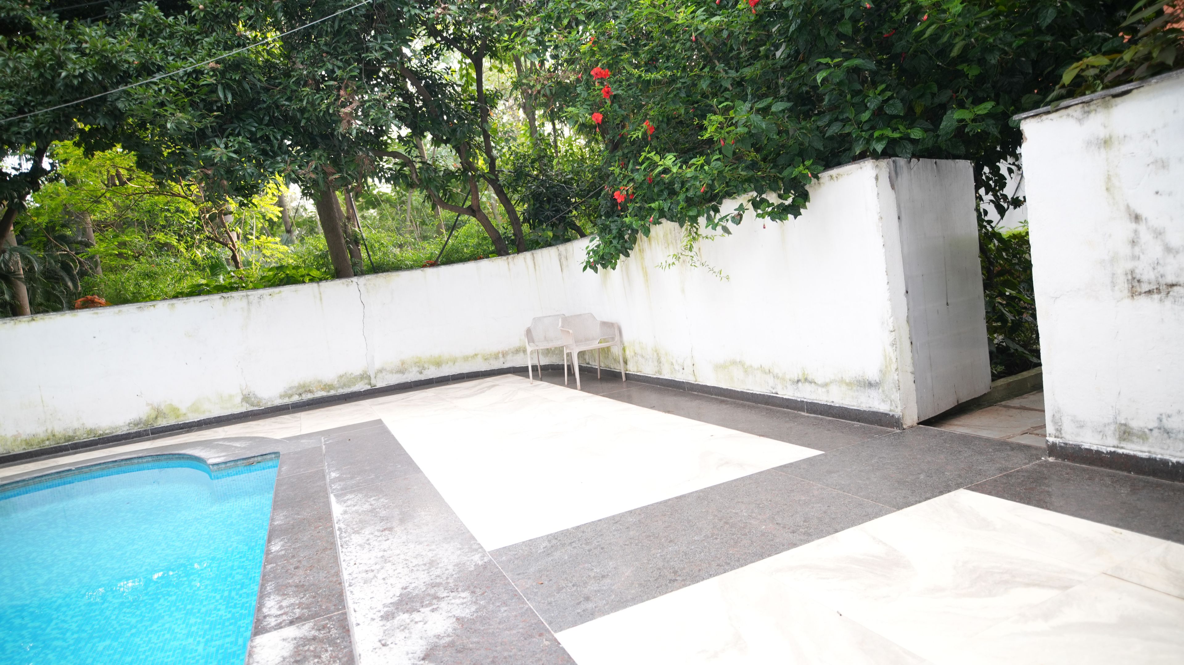 Piscina com deck em ladrilho branco e cinza, parede branca e cadeira de plástico.