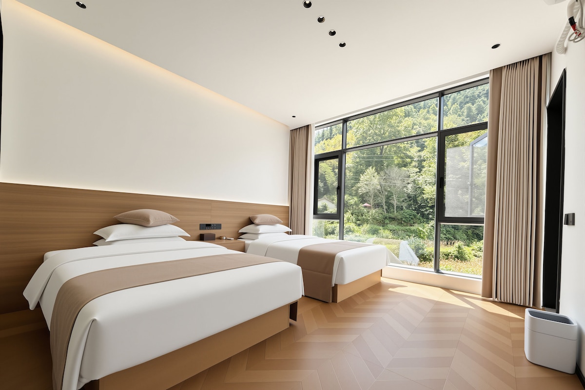 Quarto de hotel com duas camas, uma janela grande e design moderno.