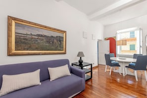 Uma sala de estar com sofá, mesa e cadeiras, luminária e quadro na parede.