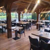 Um espaço de refeições interno com mesas e cadeiras de madeira, janelas amplas e luminárias pendentes.