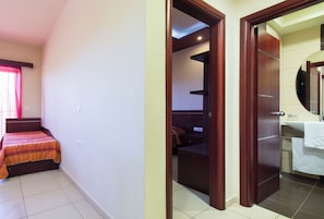 Quarto com cama, janela com cortinas e banheiro com pia e espelho.