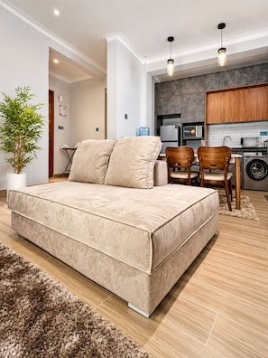 Quarto moderno com uma cama grande, um pequeno espaço de refeições com cadeiras e uma cozinha equipada.