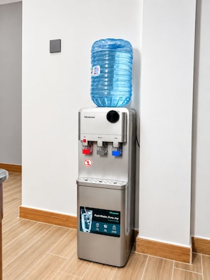 Dispensador de água com uma garrafa grande no topo, painel de controle com configurações de temperatura e um aviso de proibição de fumar.