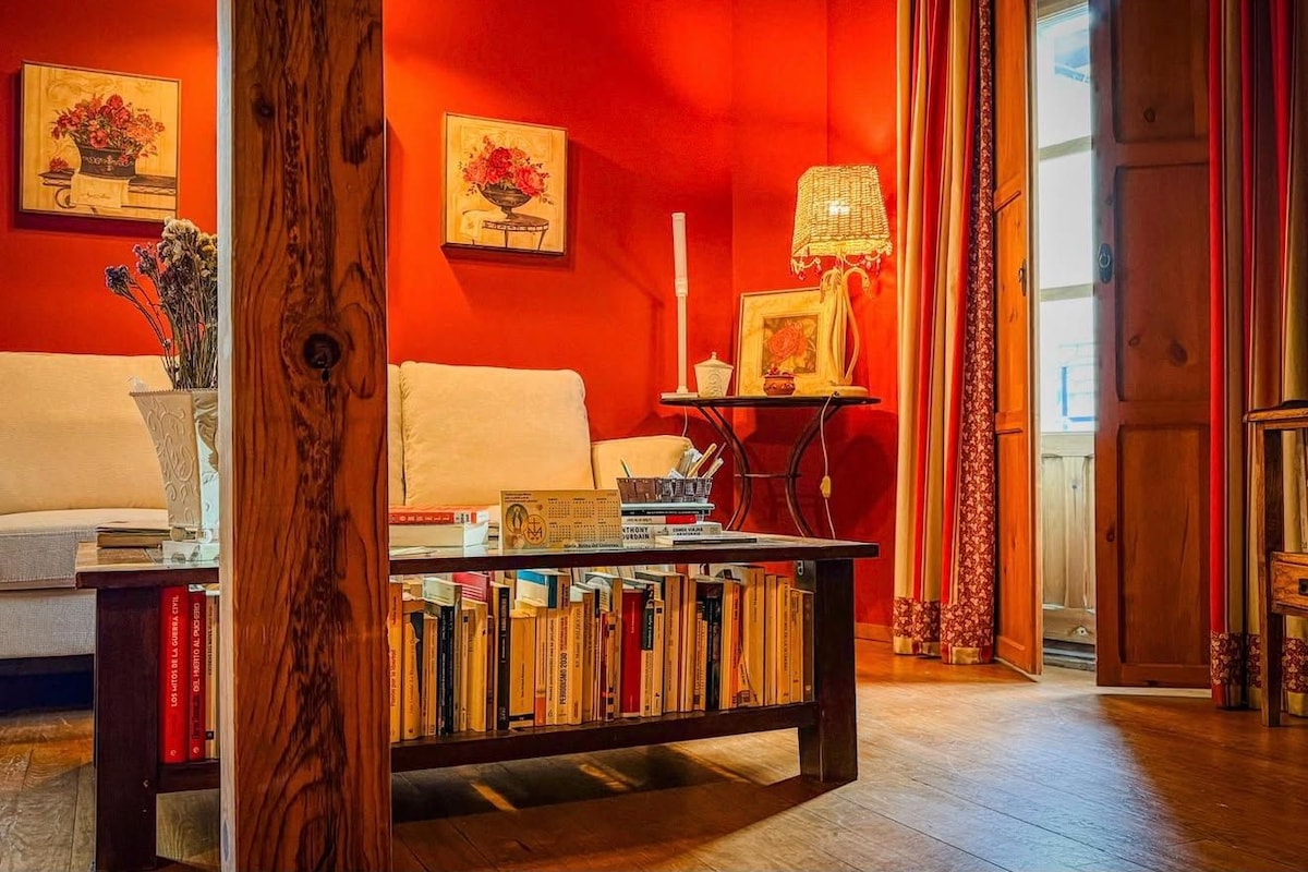 Uma sala de estar aconchegante com parede vermelha, um sofá, uma mesa de centro com livros e uma luminária.