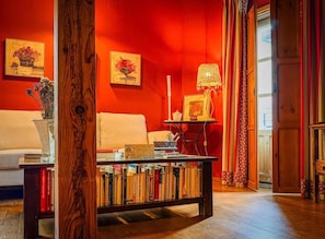 Uma sala de estar aconchegante com parede vermelha, um sofá, uma mesa de centro com livros e uma luminária.