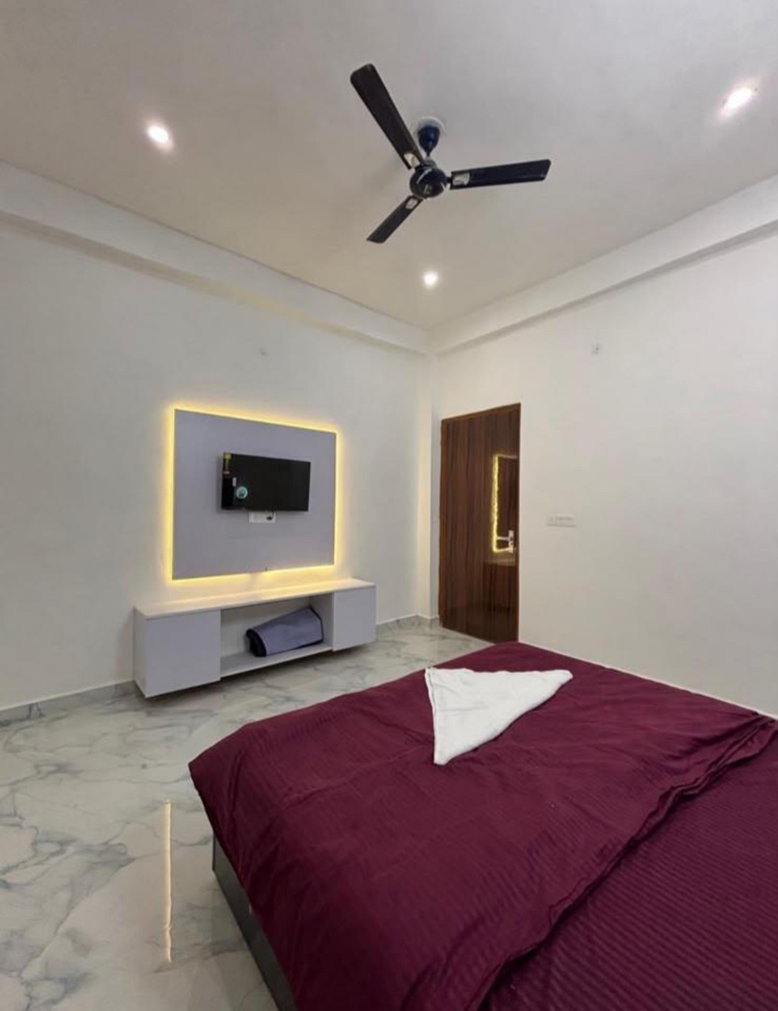 Quarto moderno com cama, ventilador de teto, televisão na parede e porta de madeira.