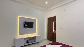 Quarto moderno com cama, ventilador de teto, televisão na parede e porta de madeira.