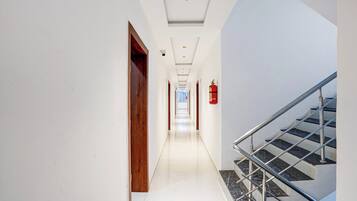 Um corredor longo e estreito, com uma porta de madeira à esquerda e uma escada à direita.