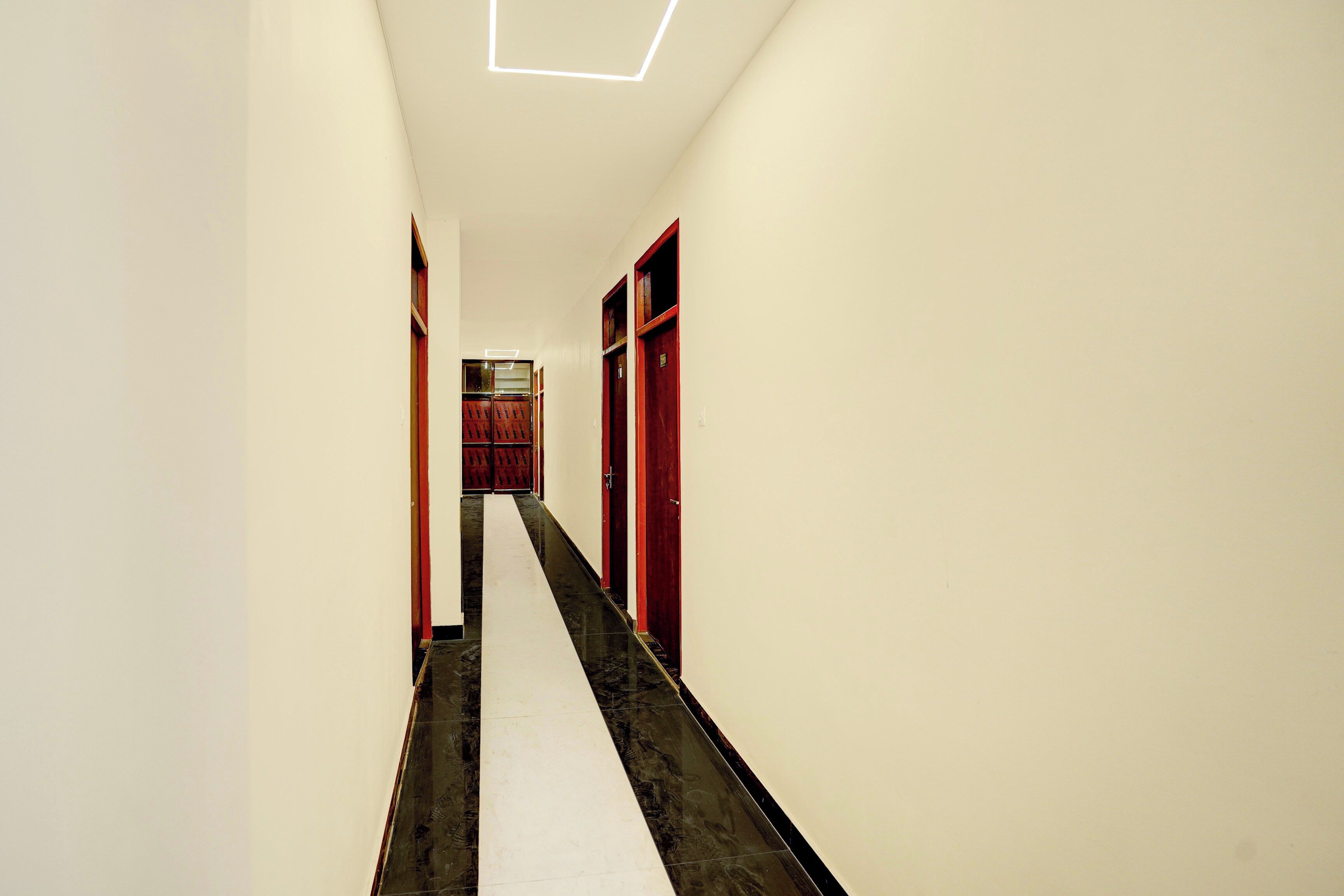 Um corredor estreito com piso branco, portas vermelhas e teto com iluminação embutida.