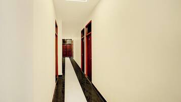 Um corredor estreito com piso branco, portas vermelhas e teto com iluminação embutida.