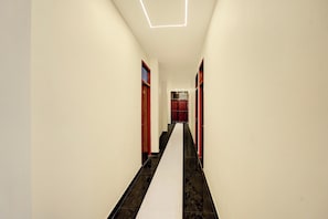 Um corredor com piso preto e branco listrado, paredes brancas e portas com moldura vermelha.