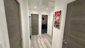 Um corredor com portas de madeira, piso de azulejos e um quadro na parede.
