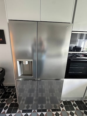 Uma geladeira de aço inoxidável com dispensador de água, situada em uma cozinha com piso estampado em padrão geométrico.