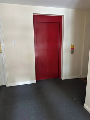 Uma porta vermelha com um aviso de segurança, um interruptor de luz e um chão escuro.