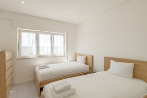 Quarto com duas camas, uma cômoda e uma janela.