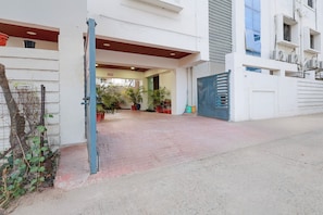 Uma entrada protegida por grades para um edifício, com um caminho de entrada pavimentado, vasos de plantas e um portão de metal.