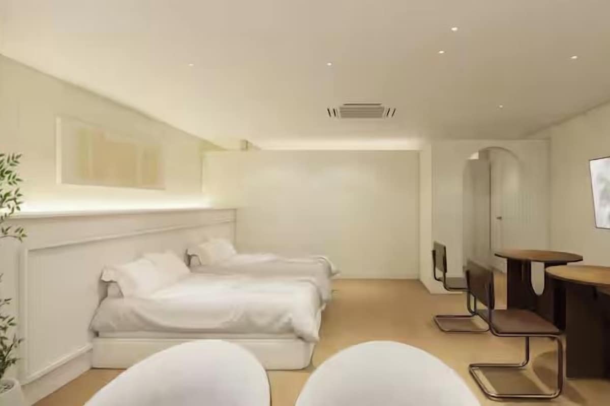 Quarto de hotel com duas camas, área de estar, televisão e uma planta.