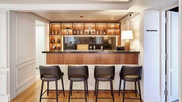 Uma área de bar com balcão de madeira, banquetas e diversas garrafas.