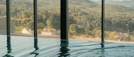 Piscina interna com vista para uma paisagem montanhosa através de amplas janelas.