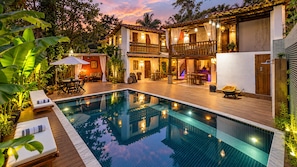 Piscina com deck de madeira, espreguiçadeiras e área de estar externa.