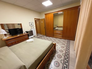 Quarto de hotel com cama, televisão, penteadeira, espelho e guarda-roupa.