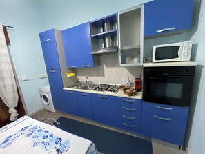 Cozinha compacta com armários azuis, fogão a gás, micro-ondas e máquina de lavar.