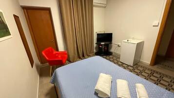Quarto de hotel com cama, televisão, pequena escrivaninha, cadeira vermelha e banheiro.