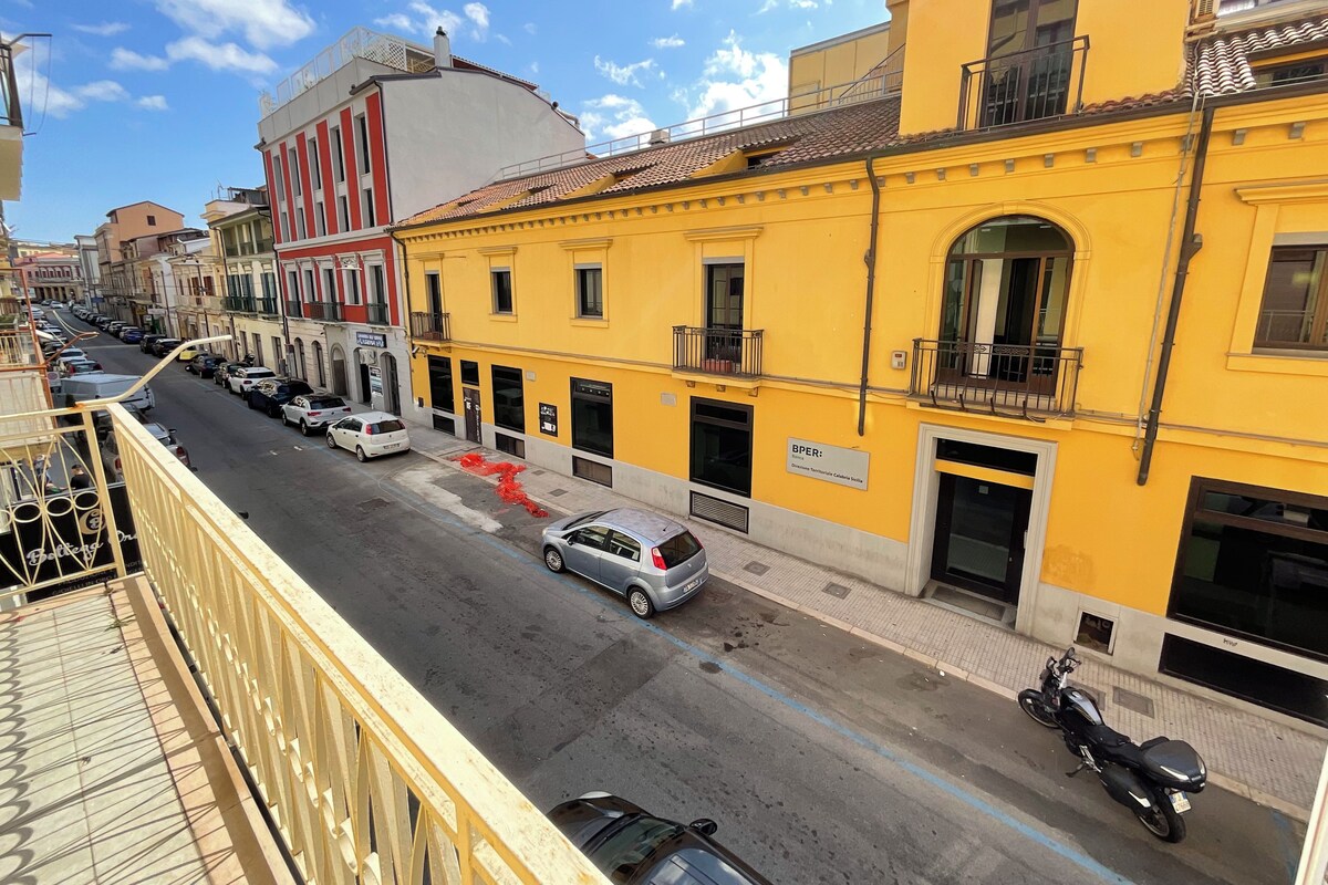 Vista da rua com edifícios amarelos, carros estacionados e uma motocicleta.