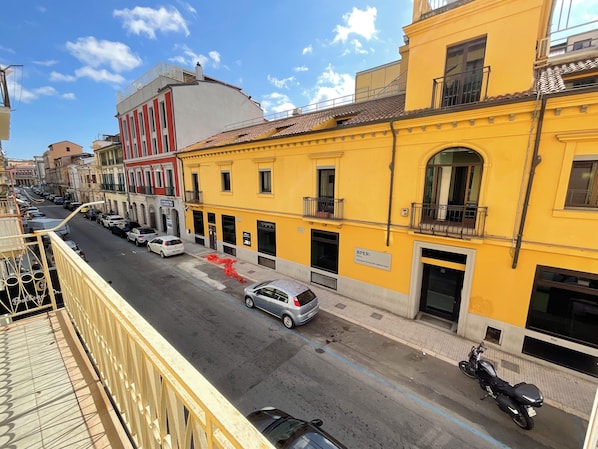Vista da rua com edifícios amarelos, carros estacionados e uma motocicleta.