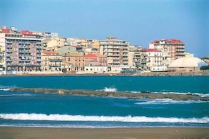 Paisagem costeira com edifícios altos, uma praia e céu azul límpido.